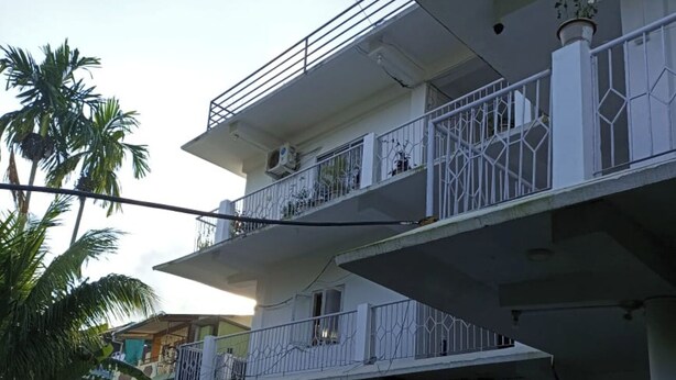 Um edifício residencial com vários andares, varandas, um carro estacionado e uma escadaria que leva à entrada.