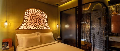 Quarto moderno com cama, chuveiro em gabinete de vidro e design de parede diferenciado.