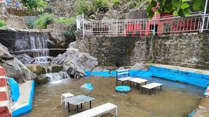 Piscina natural com bancos e uma pequena cascata, cercada por paredes de pedra e vegetação.