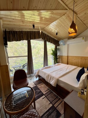 Quarto com painéis de madeira, cama, mesa, cadeira e vista para o exterior.