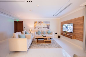 Uma sala de estar moderna com um sofá, uma mesa de centro, uma TV fixada em um painel de madeira e um quadro na parede.