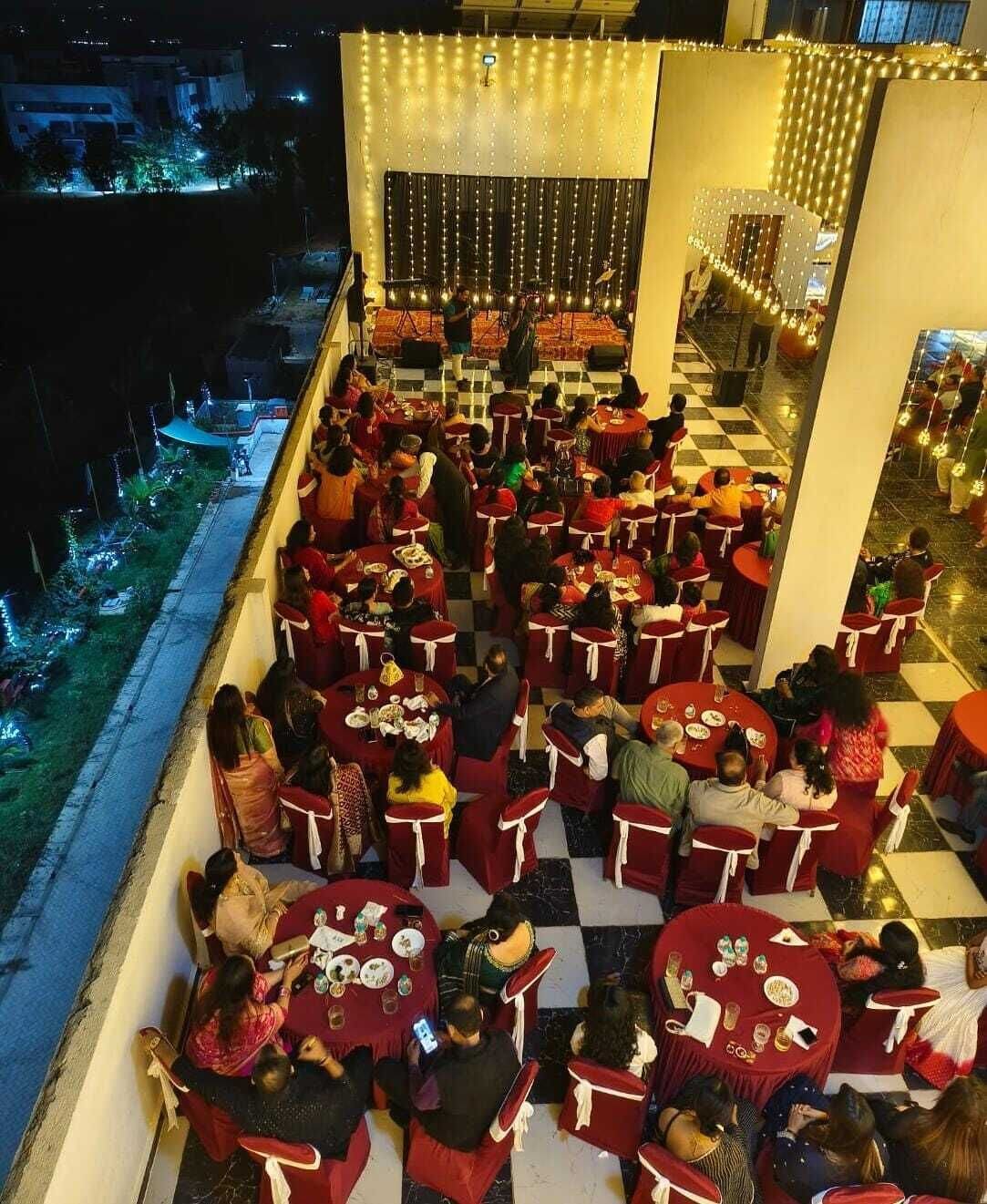Uma área de refeições ao ar livre com várias mesas e cadeiras redondas, palco para música ao vivo e vista dos arredores.
