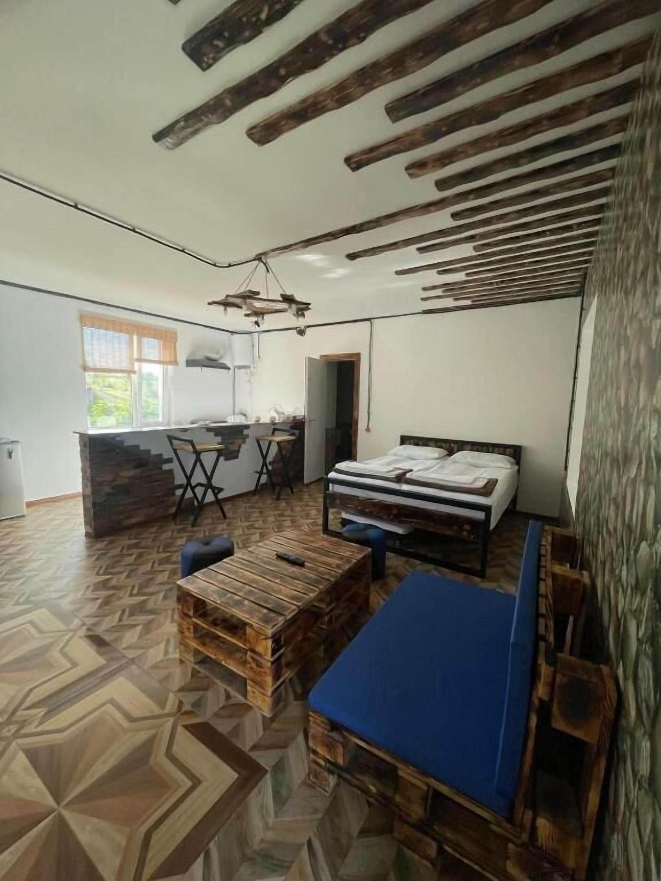 Quarto com cama, sofá azul, mesa de centro de madeira e área de cozinha com janela.