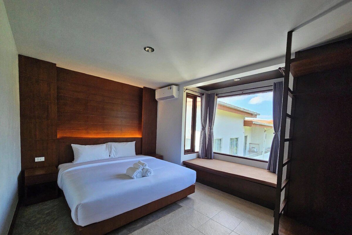 Quarto de hotel com uma cama grande, janela com cortinas, guarda-roupa embutido e ar condicionado.