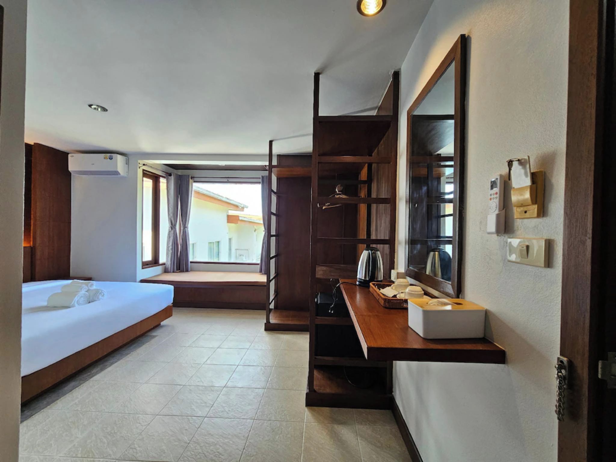 Quarto de hotel com cama, escrivaninha com espelho, guarda-roupa e janela com cortinas.