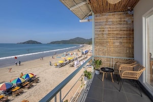 Varanda com mobiliário de vime, vista para uma praia com guarda-sóis e espreguiçadeiras.