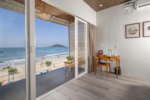 Quarto com uma grande porta de correr de vidro que dá para uma varanda com vista para a praia e o oceano.
