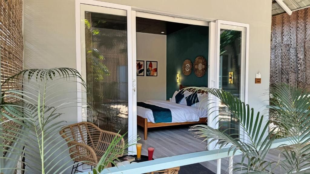 Quarto com cama, porta de vidro para uma varanda e vista para o exterior.