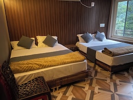 Quarto de hotel com duas camas, piso de madeira e janela com vista para área verde.