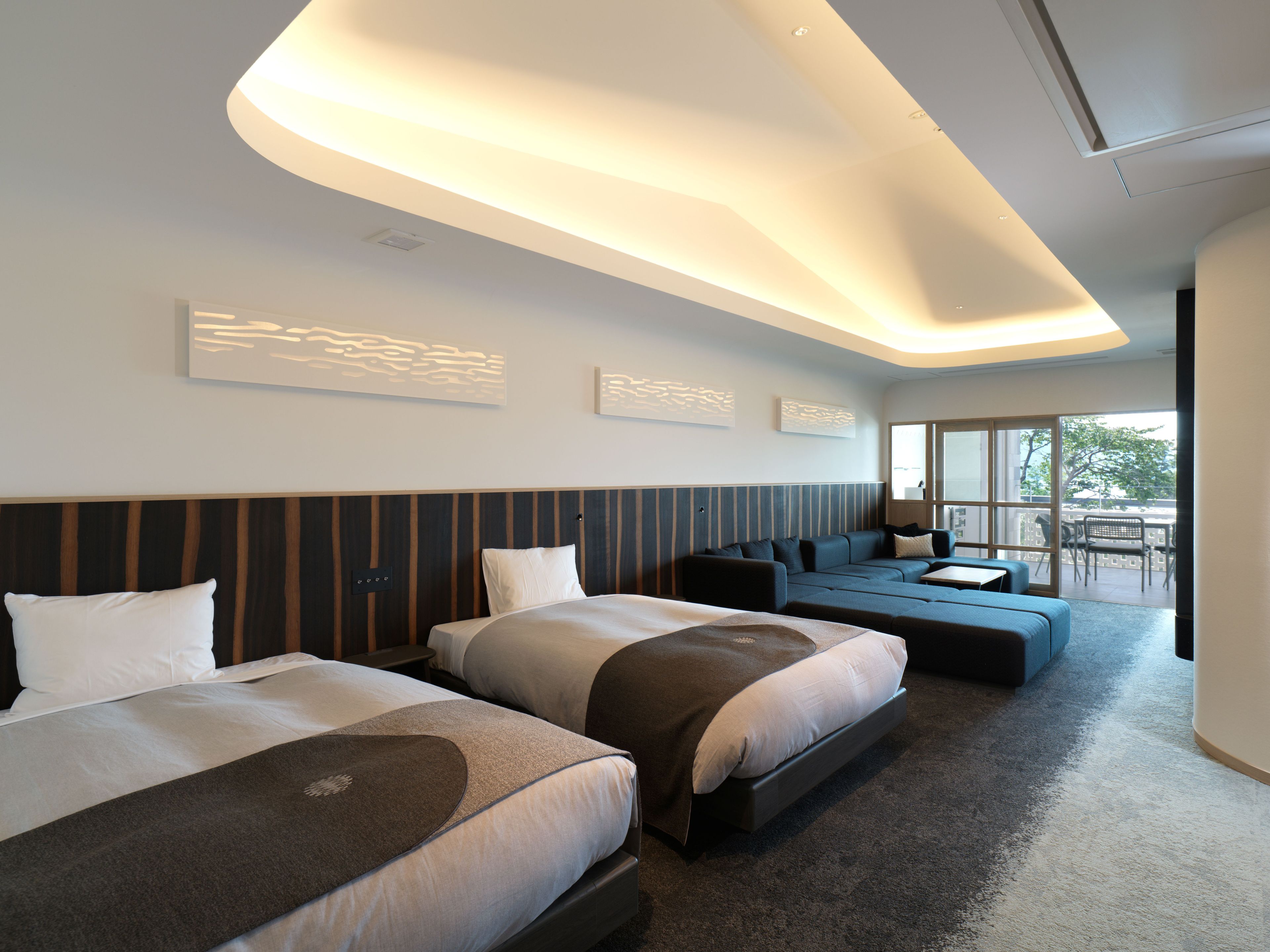 Quarto de hotel moderno com duas camas, um sofá e varanda com área de estar externa.