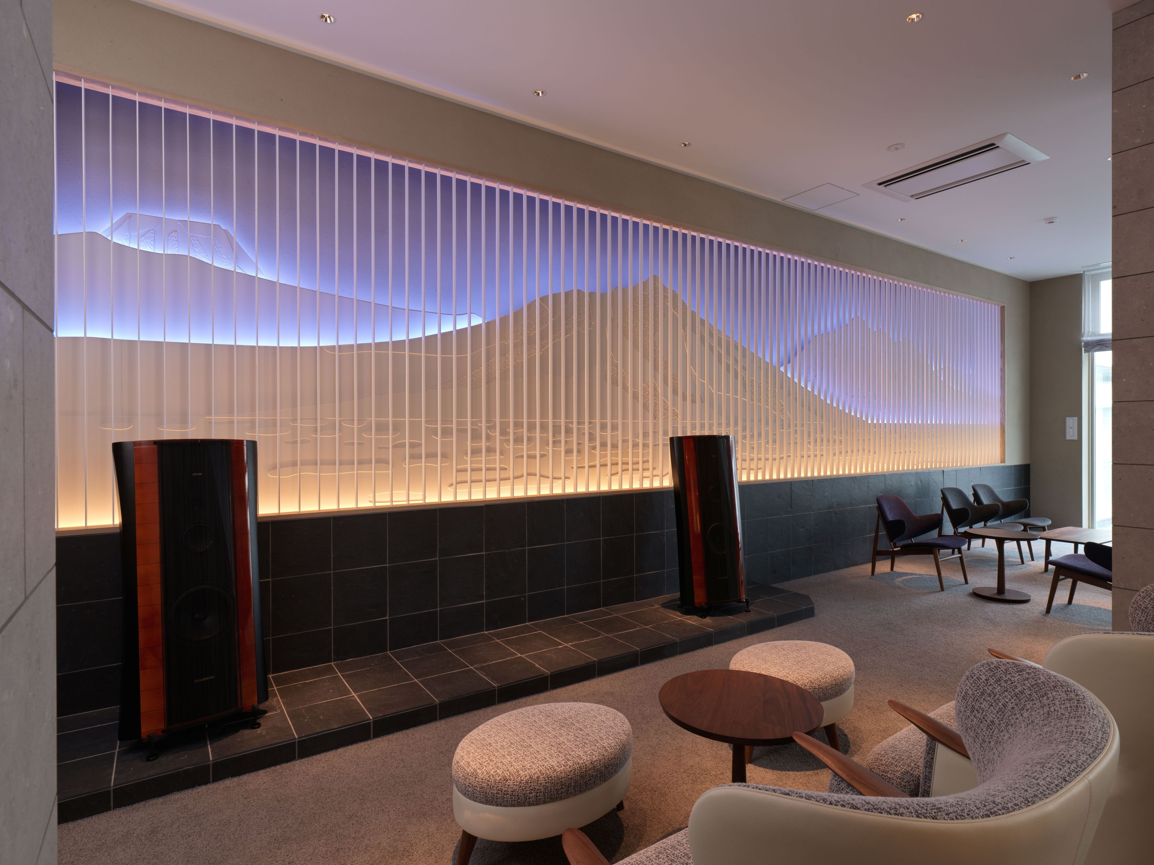 Um lobby moderno com área de estar, parede decorativa com painéis verticais e uma grande janela.