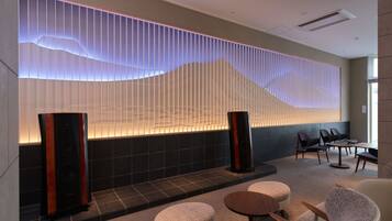 Um lobby moderno com área de estar, parede decorativa com painéis verticais e uma grande janela.