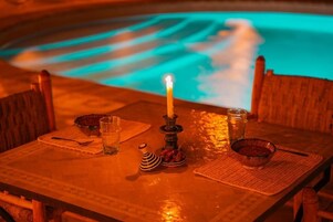Mesa com vela, copos e tigela, com uma piscina azul ao fundo.