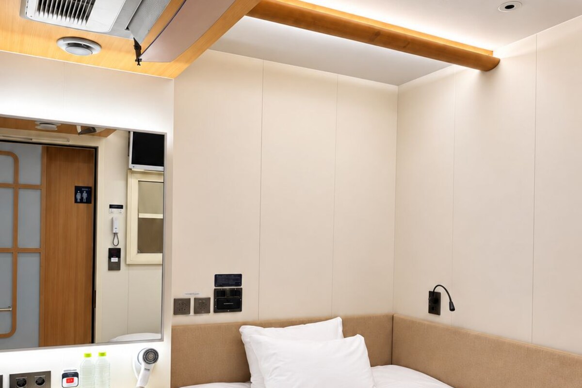 Quarto de hotel com cama, escrivaninha, espelho, sanita e área de duche.