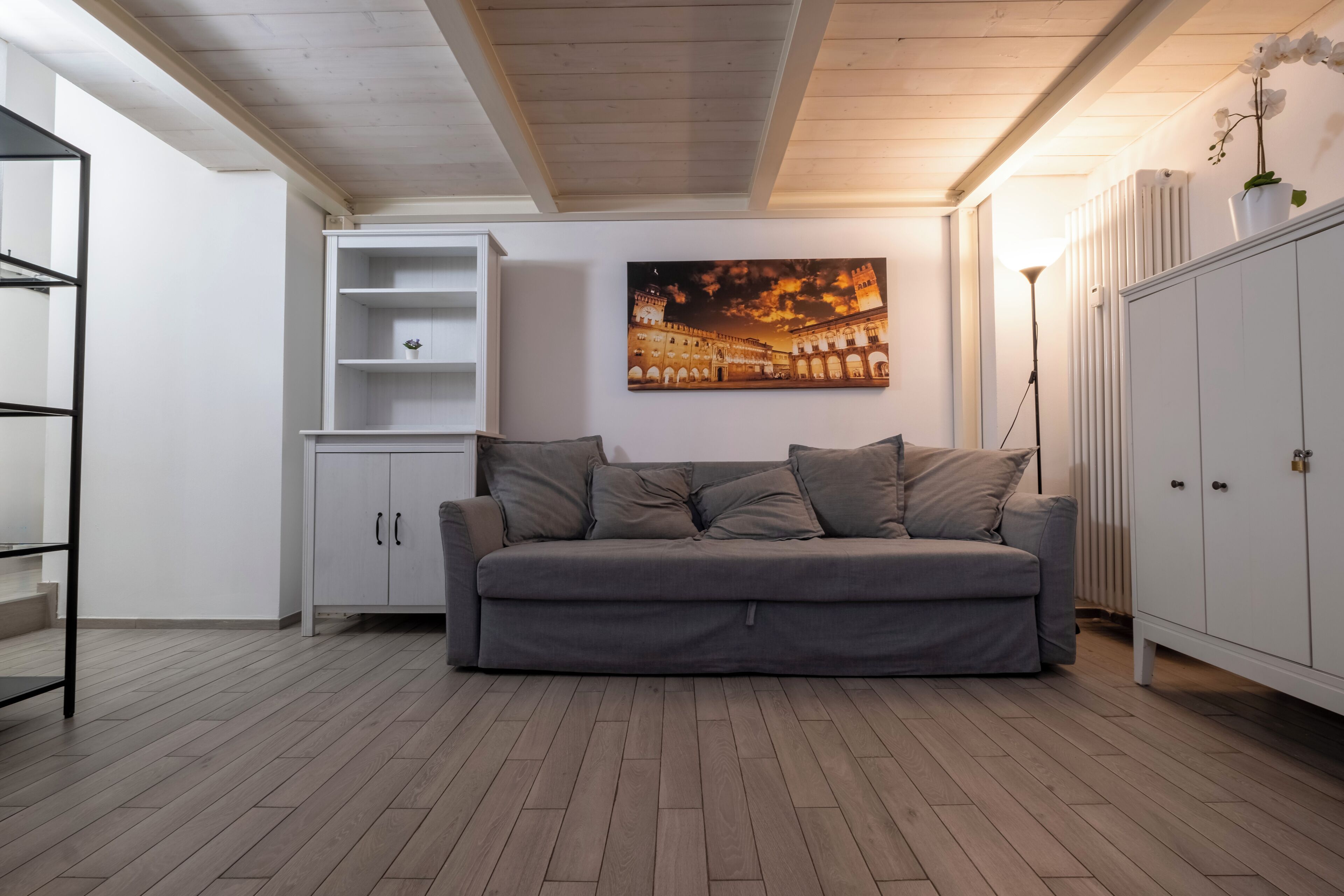 Uma sala de estar moderna com um sofá cinzento, uma estante branca e um quadro grande emoldurado na parede.