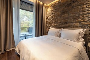 Quarto com parede de pedra, uma cama grande e vista para uma varanda.
