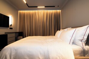 Quarto de hotel com uma cama grande, televisão de tela plana na parede e uma cortina.