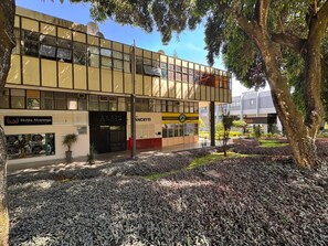 Um edifício moderno com fachada de vidro, fachada escura e área ajardinada com arbustos e cascalho.