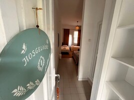 Corredor que leva a um quarto com cama, luminária pendente e porta-toalhas.