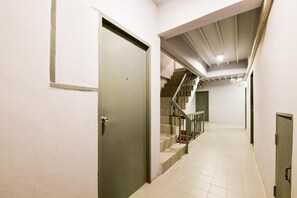 Um corredor com uma porta à esquerda, uma escada com guarda-corpo de metal e chão em azulejo.