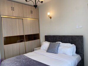 Quarto com cama, guarda-roupa e luminária fixada na parede.