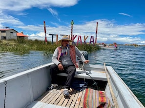 Uma pessoa sentada em um barco, com vista para um canal e um edifício com a palavra 'TIKAYAK' ao fundo.