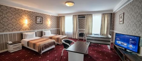 Quarto de hotel com duas camas, uma escrivaninha, televisão e janela com cortinas.