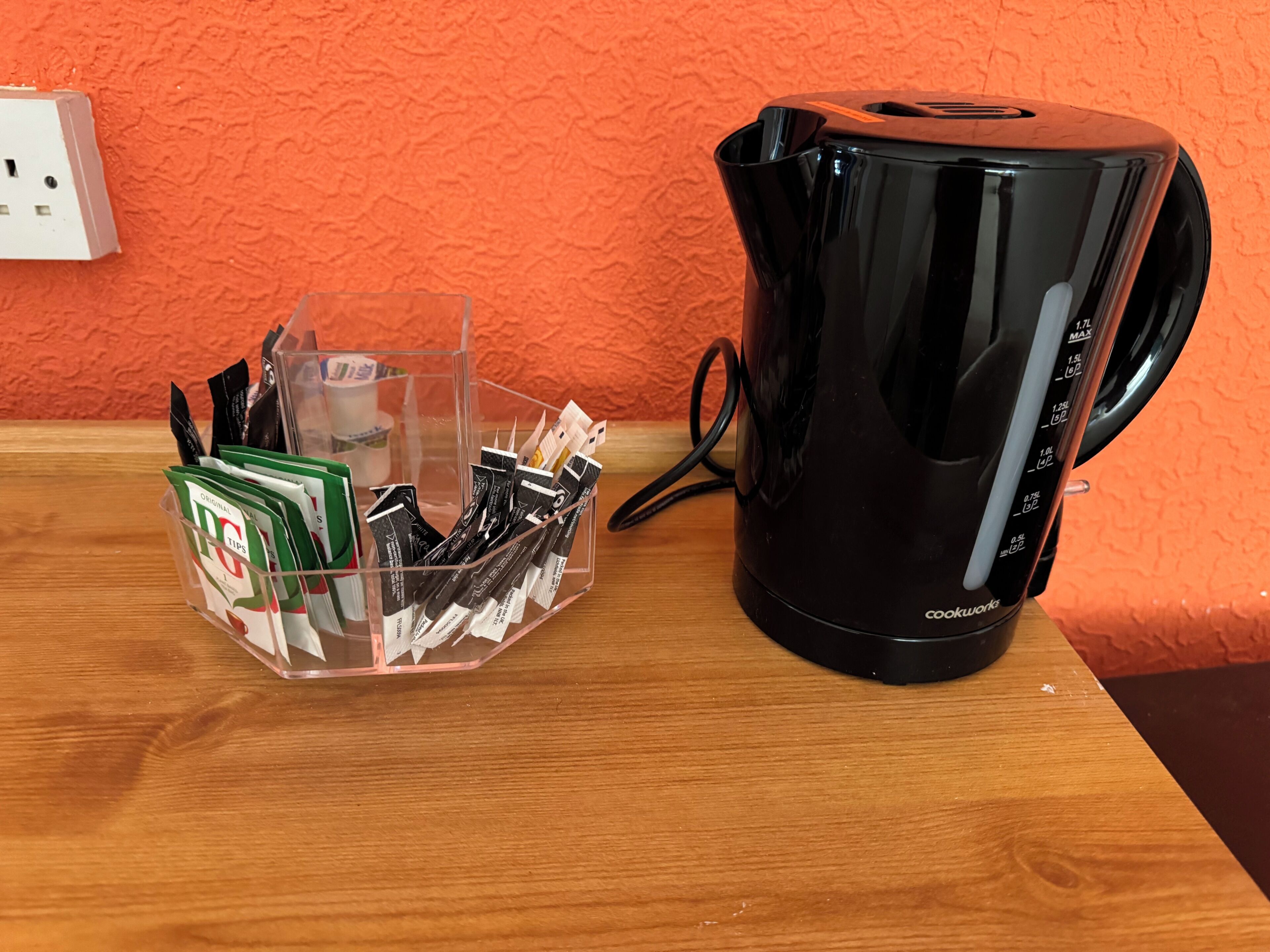Uma cafeteira preta sobre uma mesa de madeira, com um recipiente de plástico transparente contendo diferentes cápsulas de café.