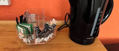 Uma cafeteira preta sobre uma mesa de madeira, com um recipiente de plástico transparente contendo diferentes cápsulas de café.
