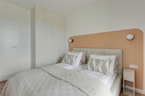 Quarto com cama, duas mesas de cabeceira, guarda-roupa e luminária na parede.