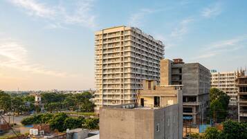 Edifício residencial de vários andares com varandas, cercado por vegetação e outros edifícios.