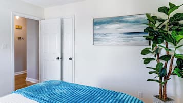 Um quarto com cama, porta, um quadro e uma planta em vaso.