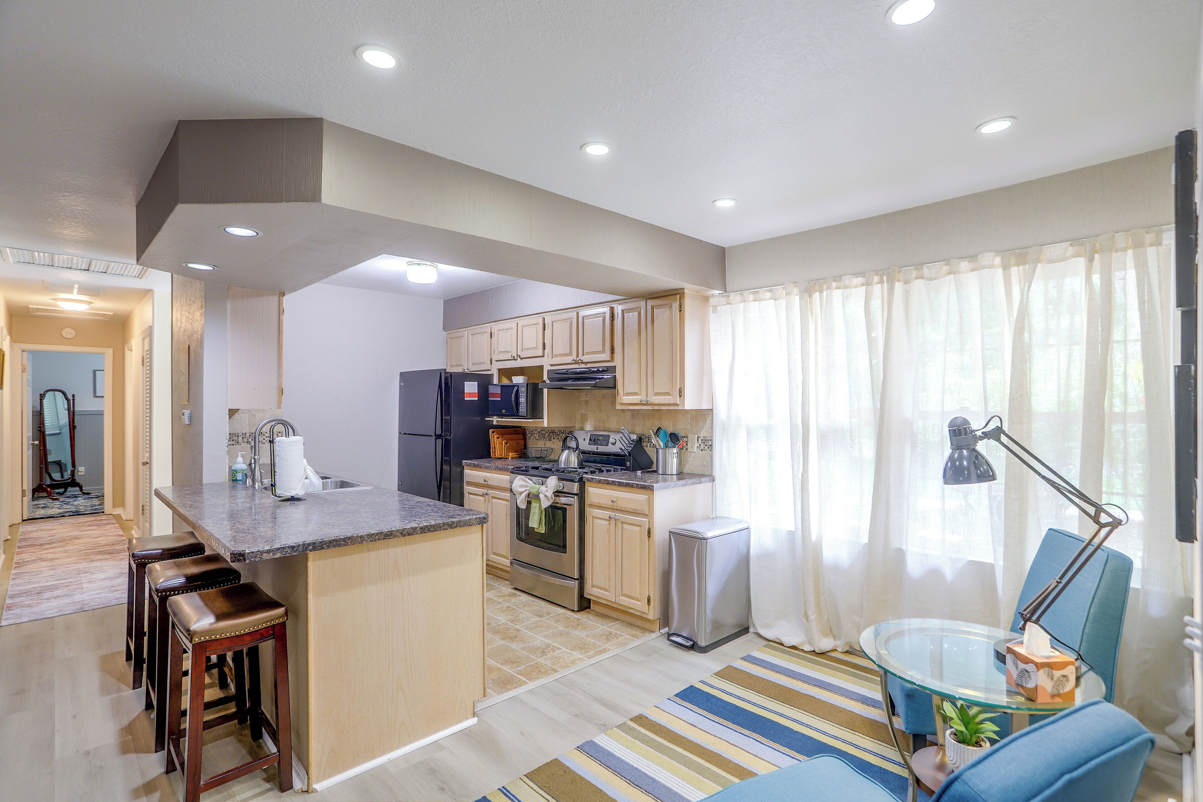 Uma cozinha moderna com ilha central, eletrodomésticos de aço inoxidável e área de jantar com mesa de vidro e cadeiras azuis.