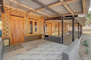 Uma área externa coberta com piso de azulejos, portas de madeira com desenhos decorativos e estrutura de telhado em metal.