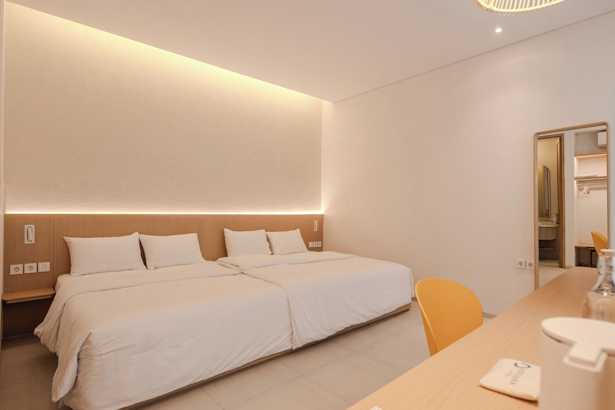 Quarto de hotel moderno com uma cama grande, mesas de cabeceira, uma escrivaninha com cadeira e luminária pendente.