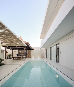 Piscina interior moderna com área de estar coberta e parede de pedra.