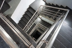 Uma escadaria com corrimão de metal e degraus pretos.