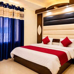 Quarto de hotel com uma cama grande, cabeceira de madeira e edredom vermelho e branco.