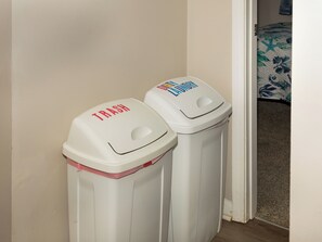 Duas lixeiras, uma com a etiqueta 'TRASH' e outra com a etiqueta 'DIRTY LAUNDRY', em um corredor.