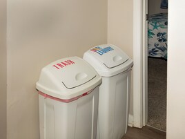 Duas lixeiras, uma com a etiqueta 'TRASH' e outra com a etiqueta 'DIRTY LAUNDRY', em um corredor.
