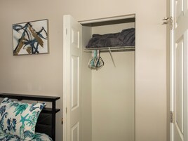 Quarto com uma cama, um guarda-roupa com roupas penduradas e um quadro na parede.