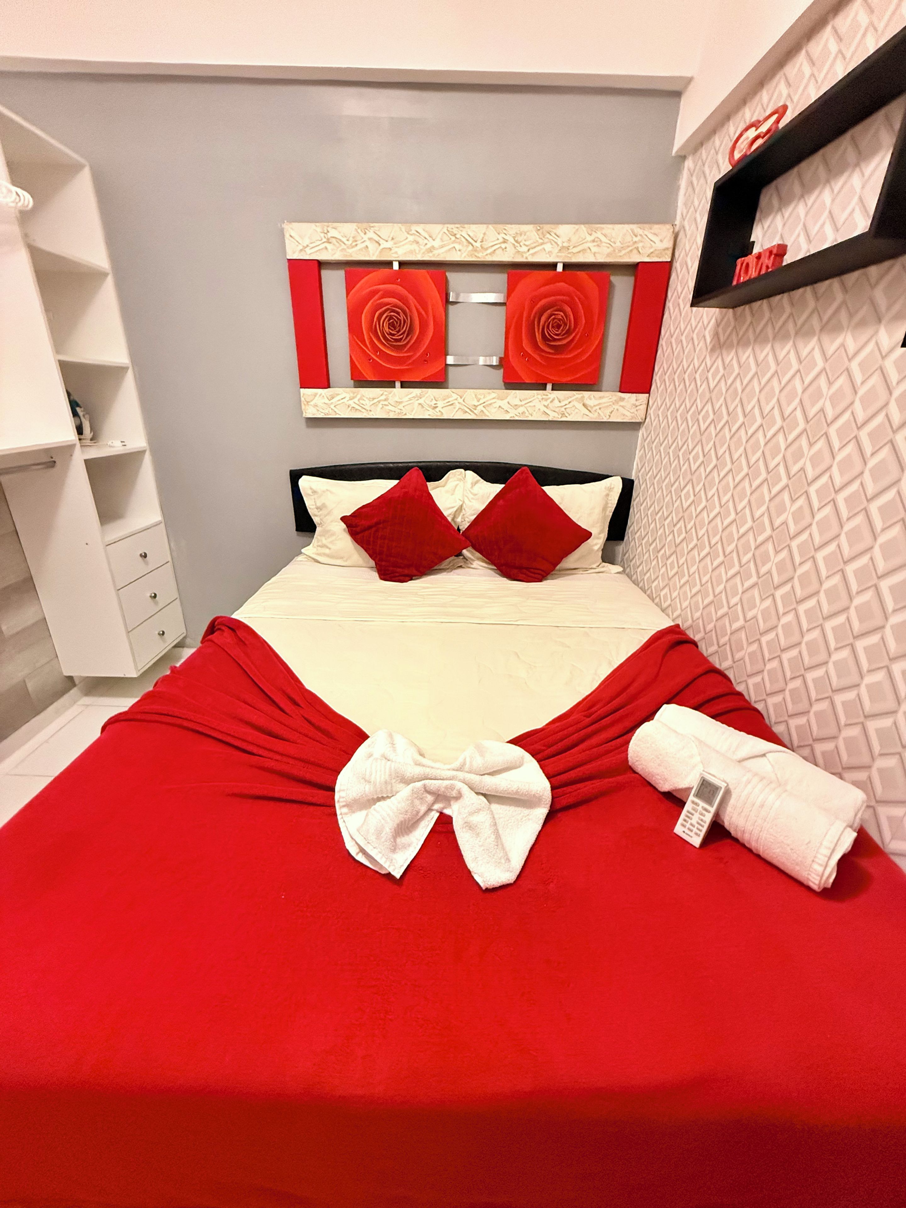 Uma cama com colcha vermelha e branca, duas almofadas vermelhas e uma toalha branca com um celular.