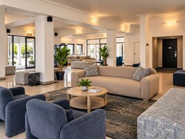 Um hall amplo com um sofá bege, poltronas azuis e uma mesa de centro redonda.