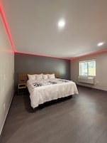 Quarto com cama, mesa de cabeceira e janela com ar condicionado.