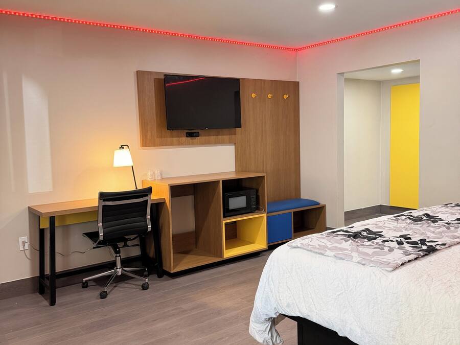 Quarto com cama, escrivaninha, cadeira, televisão e micro-ondas.