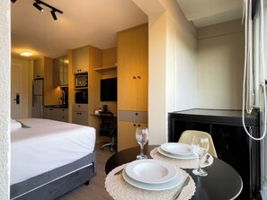 Quarto de hotel com cama, mesa de jantar posta com pratos e copos, micro-ondas, frigorífico e televisão.