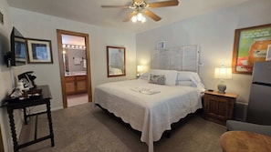 Quarto de hotel com cama, mesas de cabeceira, ventoinha no teto e geladeira.