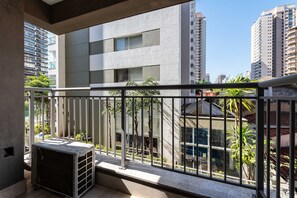 Uma varanda com vista para edifícios altos, uma mesa pequena e uma lixeira.