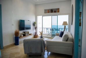 Uma sala de estar moderna com sofá, televisão e varanda com vista para o mar.