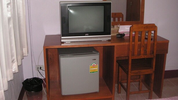 Uma mesa de madeira com uma televisão, um pequeno frigorífico e uma cadeira.